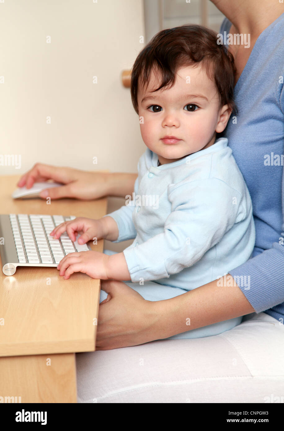 Baby sat on mums lap while shes working on computer Stock Photo - Alamy
