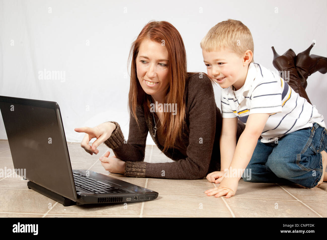 Pretty redheaded mother with her blond son one the floor with a laptop ...