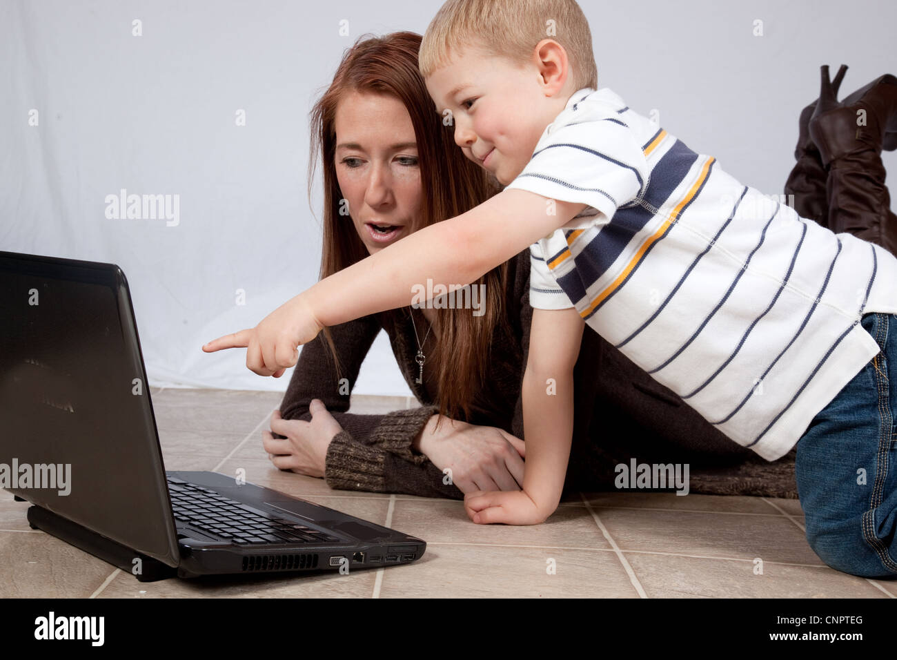 Pretty redheaded mother with her blond son one the floor with a laptop ...