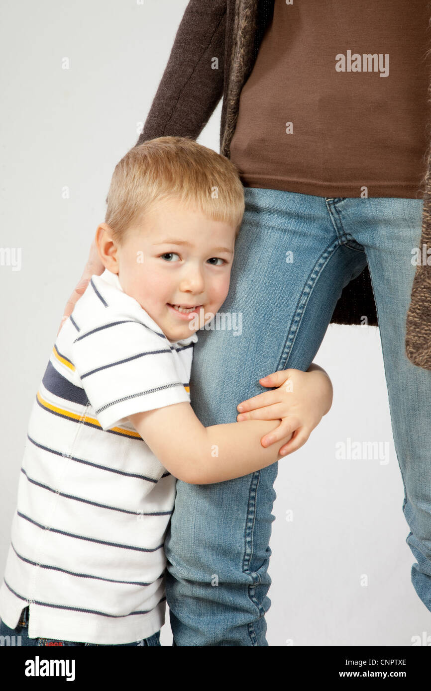 Cute blond boy hugging his mothers leg with a happy smile, and his ...