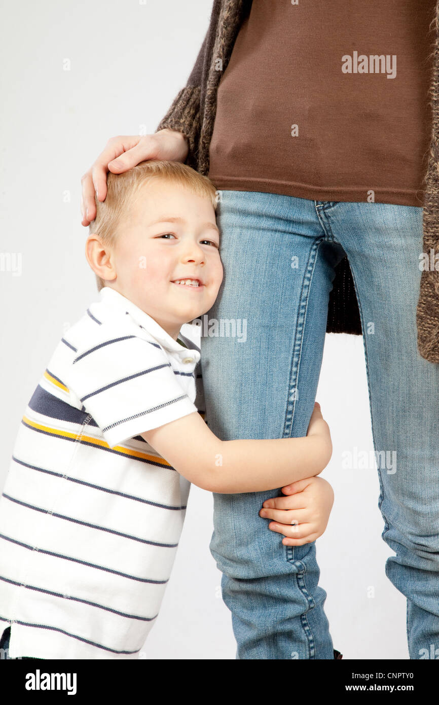 Cute blond boy hugging his mothers leg with a happy smile, and his ...