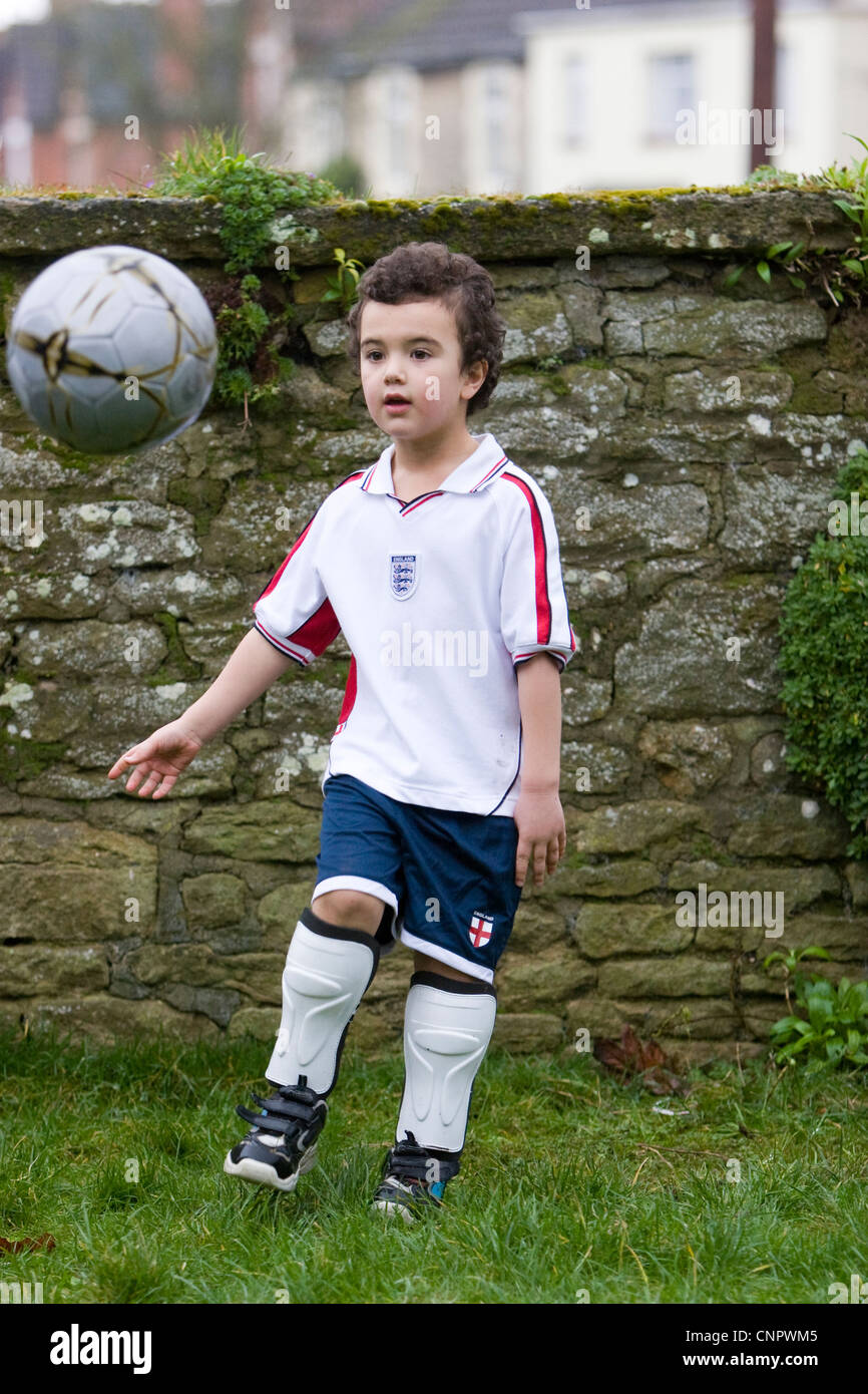 Small boy playing football in the front garden wearing his England team ...