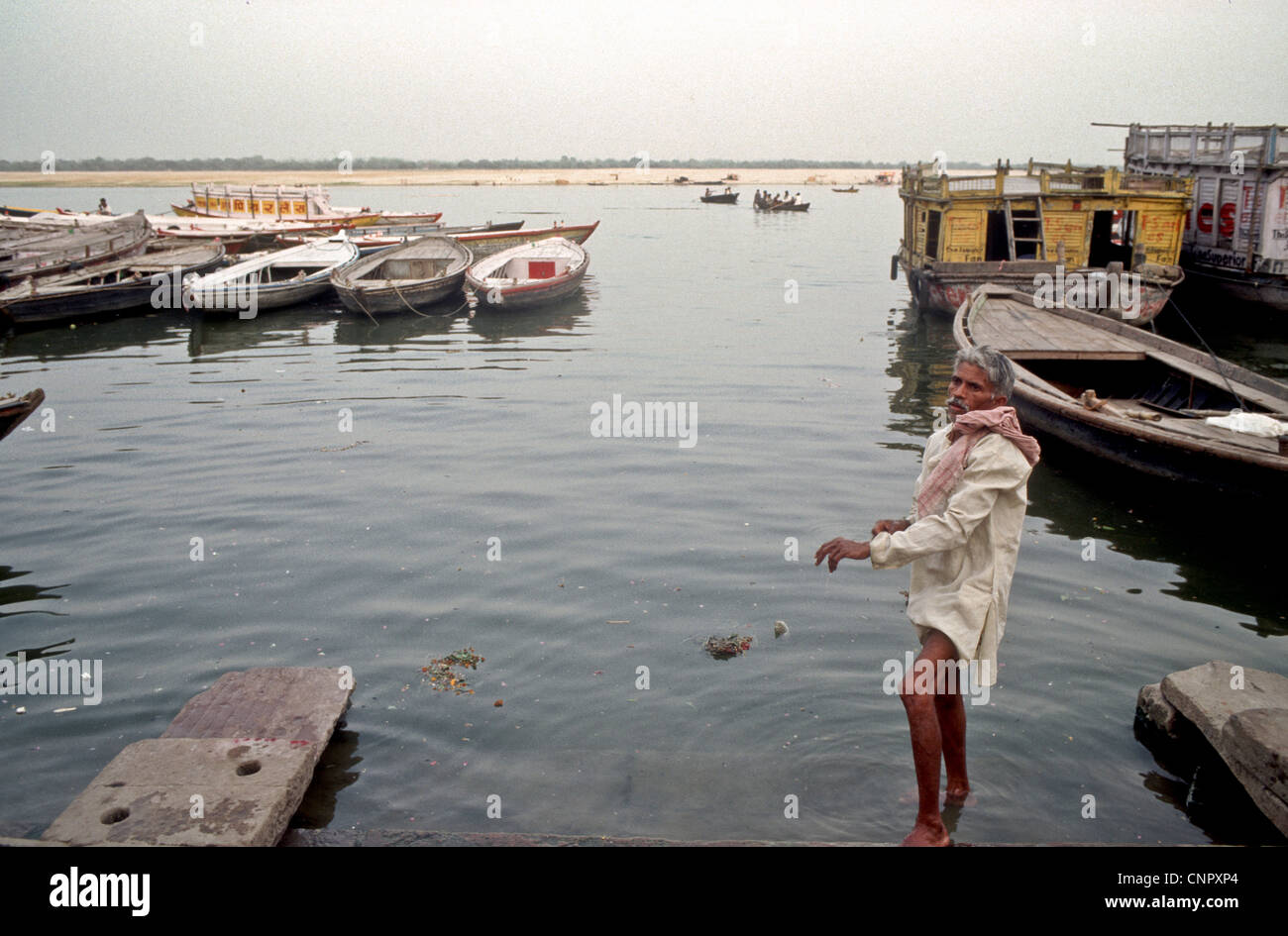 Indian man and boats moored on the banks of the Ganges at the ancient ...