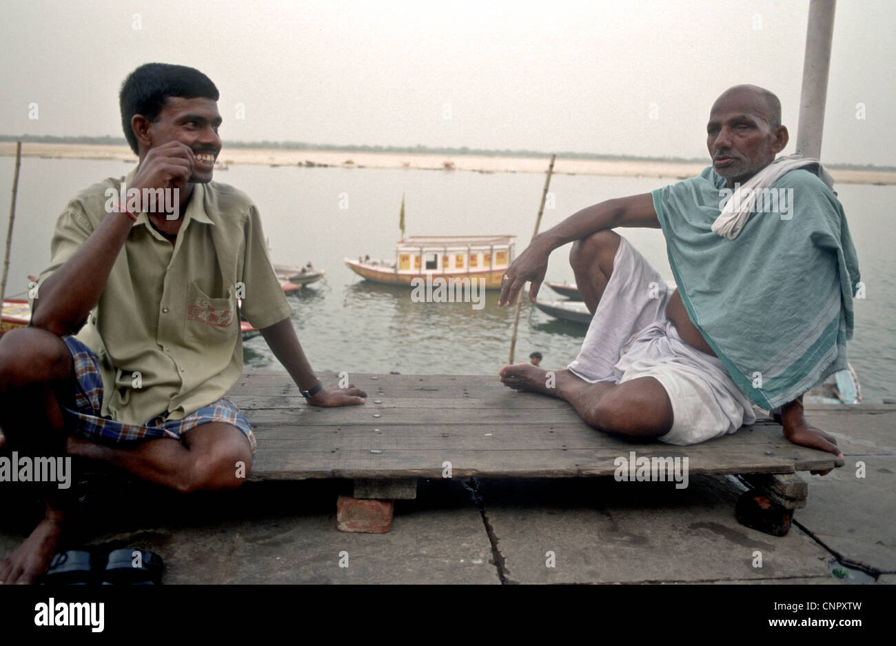 Two Indian men sitting next to river Ganges at the ancient Indian city ...