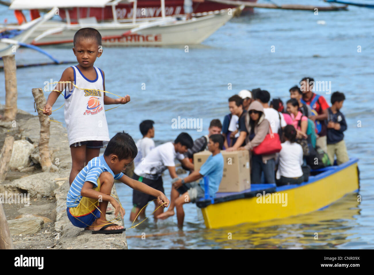 2 Filipino Asian boys sitting standing on pier while overcrowded small ...