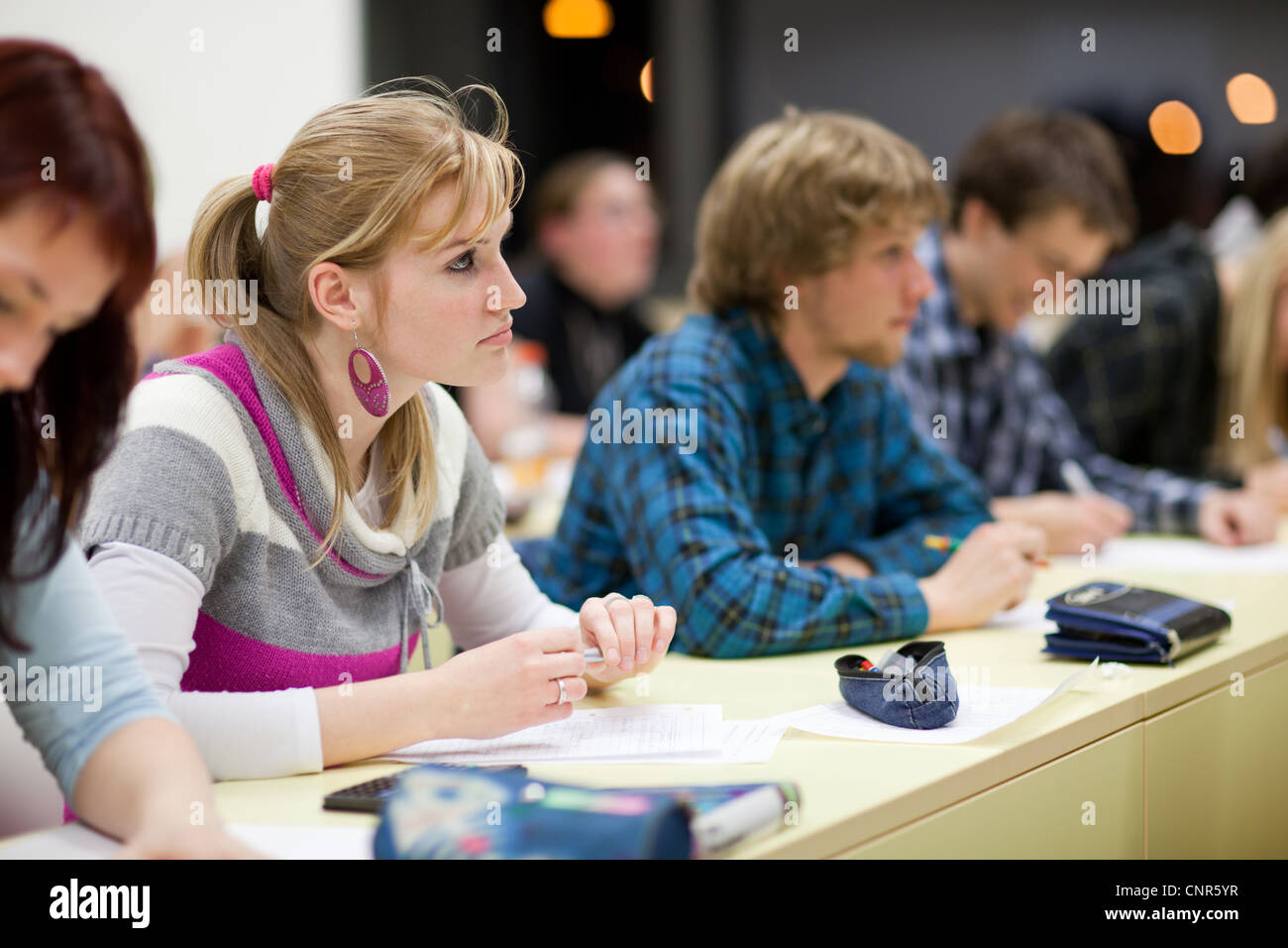 pretty female college student sitting in a classroom full of students ...