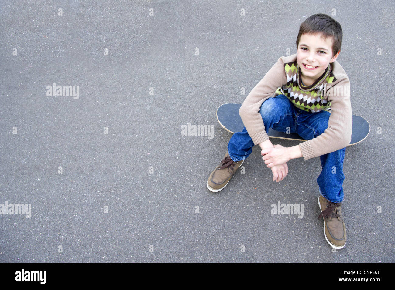 Teenage boy sitting on the skateboard on the pavement Stock Photo - Alamy