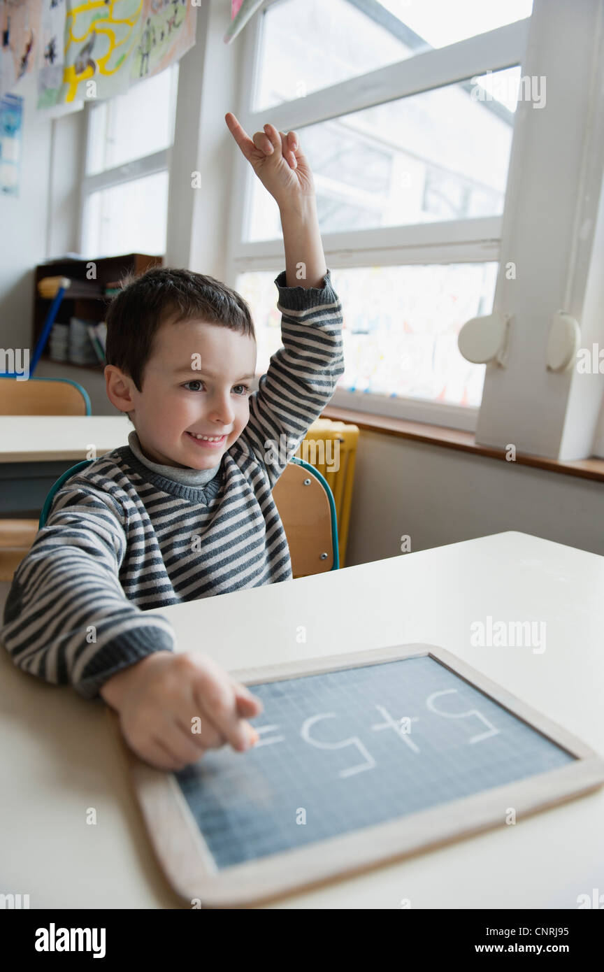 Boy sitting at desk with chalkboard, hand raised Stock Photo - Alamy