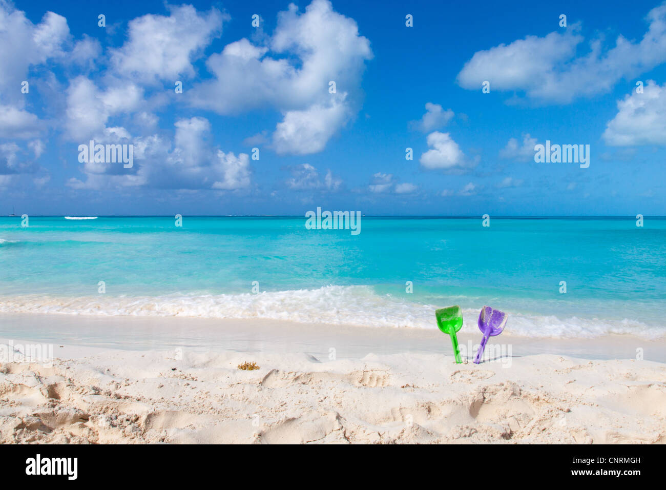 Pair of colored spades on a white sand beach in front of the sea. The ...