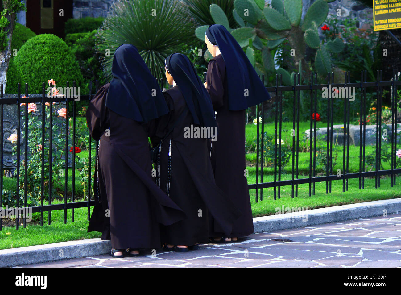 Three young nuns from behind in garden. Temple at Basilica de Guadalupe ...