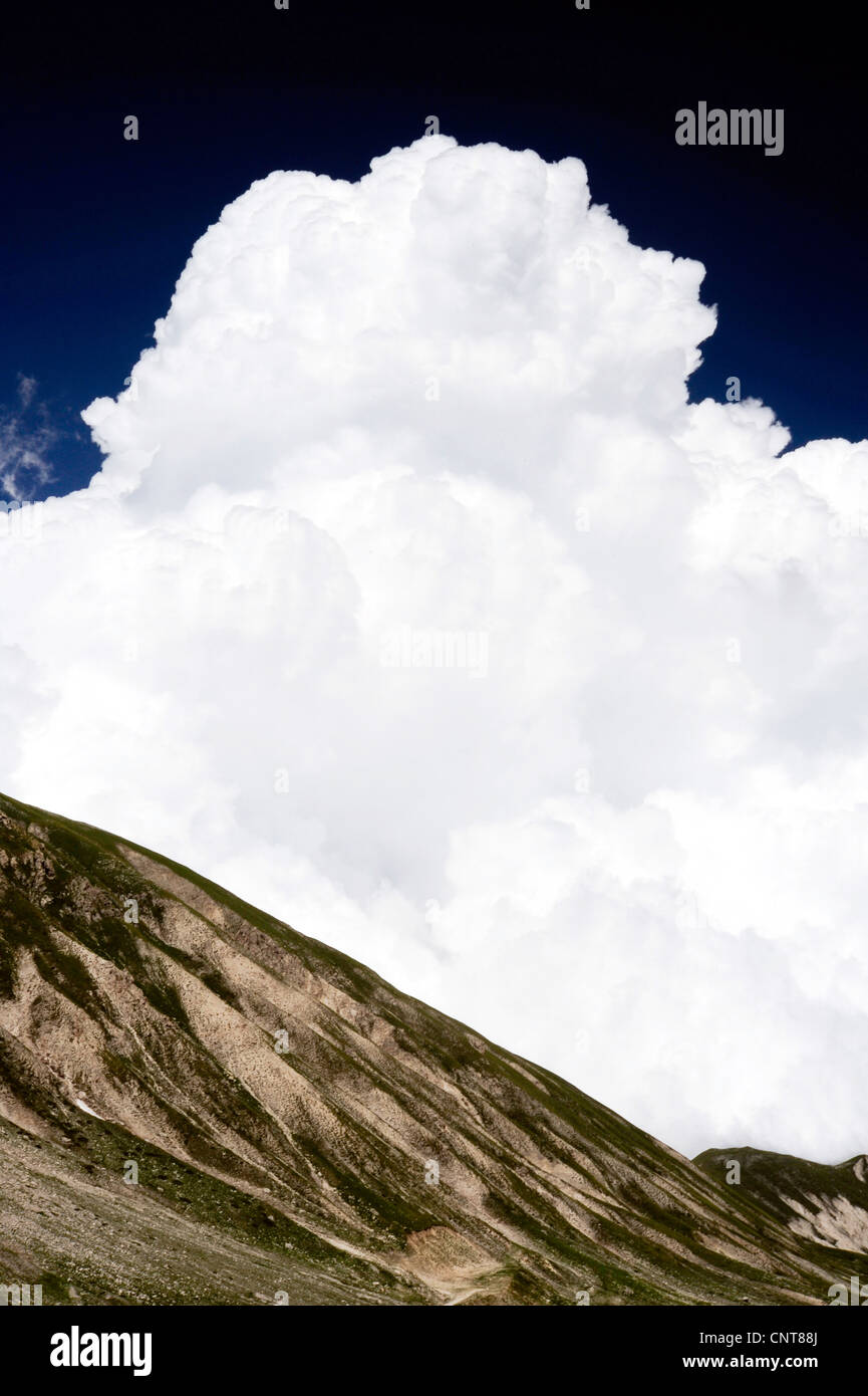 white clouds looming behind a mountain slope with dry meadows, Italy ...
