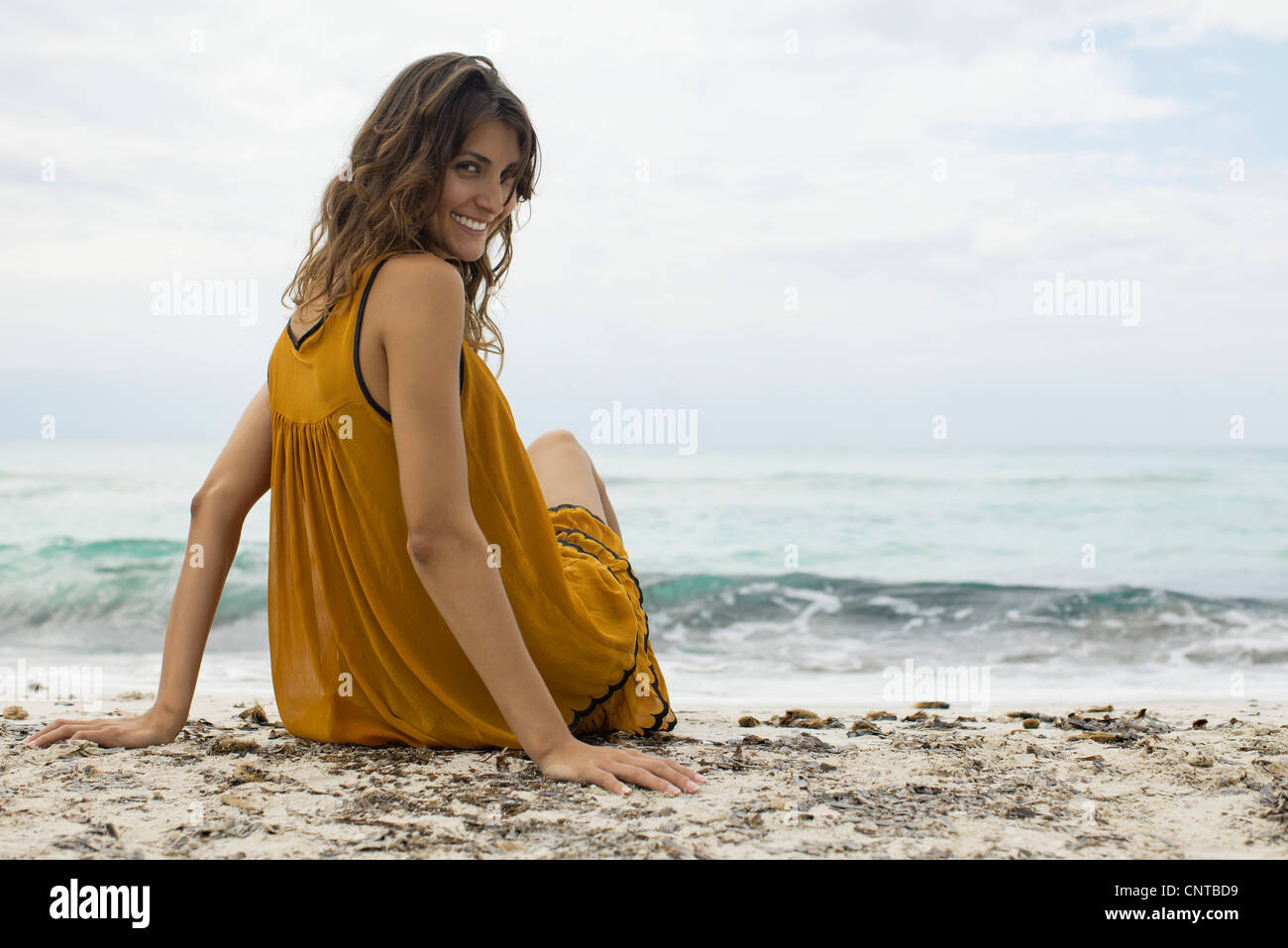 Young woman sitting on beach, looking over shoulder at camera Stock ...