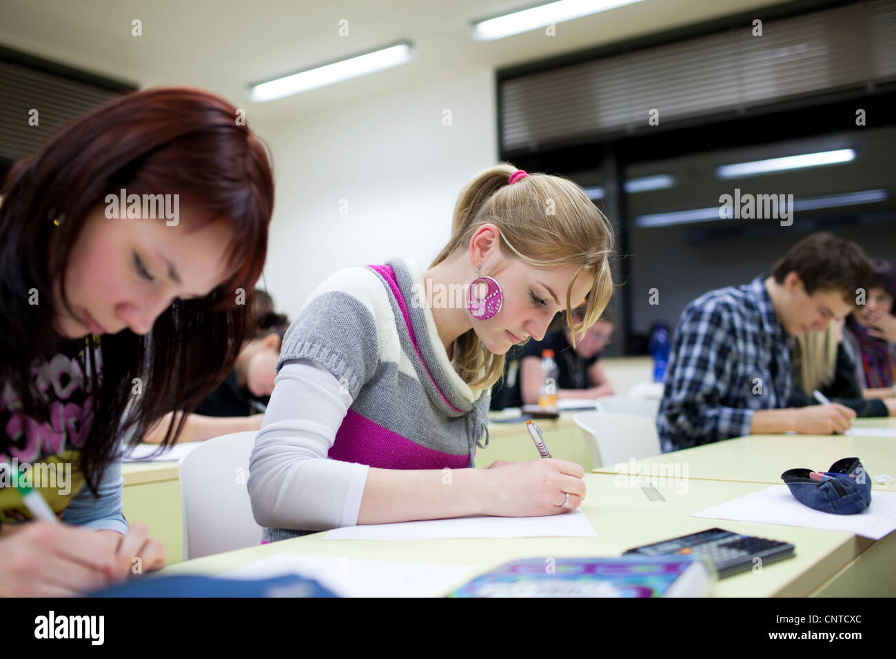 pretty female college student sitting in a classroom full of students ...