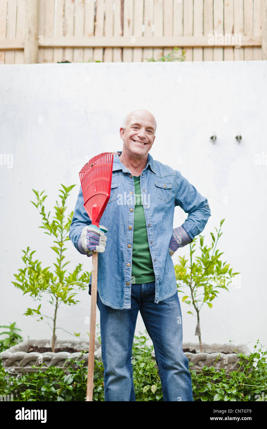 Older man holding rake in backyard Stock Photo - Alamy