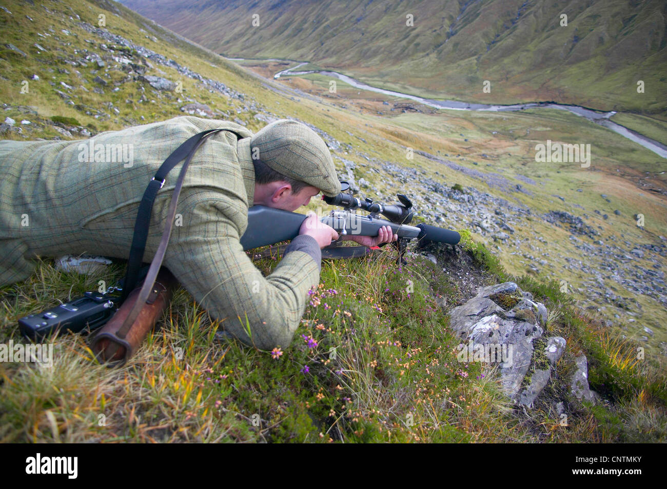 stalker lying on the belly at the edge of a mountain slope aiming down ...