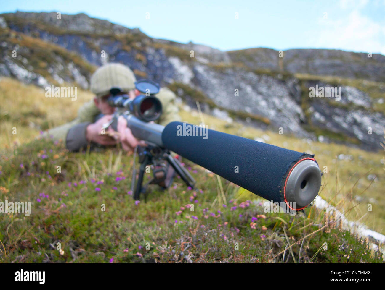stalker lying on the belly at the edge of a mountain slope aiming down ...