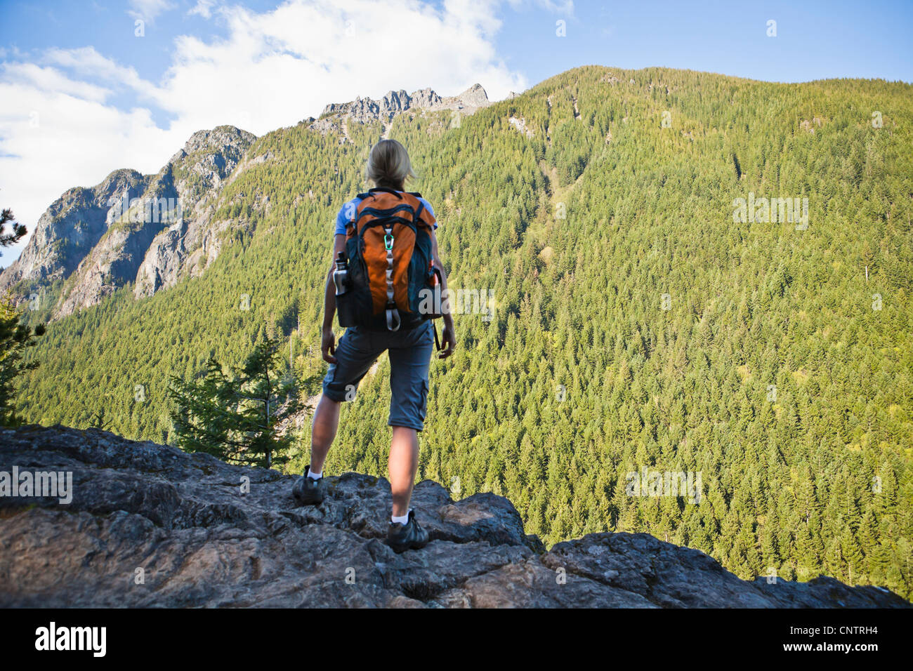 A woman hiker standing on the edge of a rocky cliff looking up at a ...