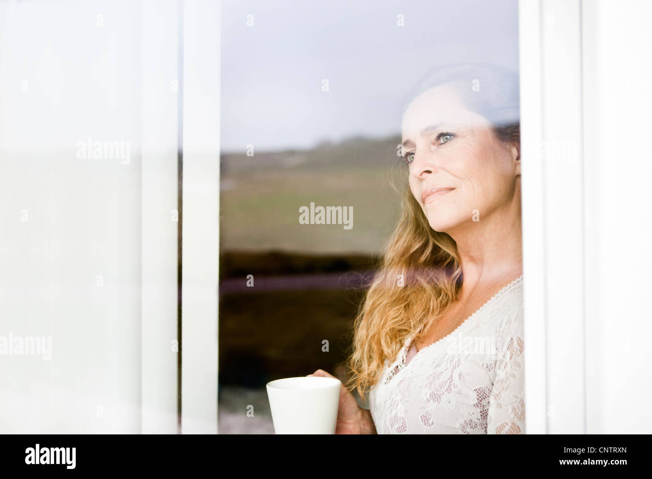 Woman having cup of coffee at window Stock Photo - Alamy