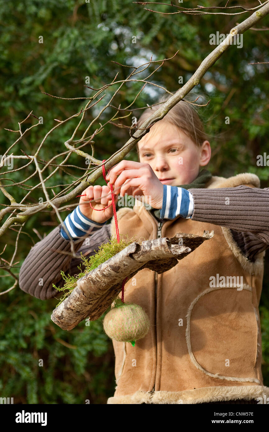 girl fixing a self-made dispenser for nesting material at a branch ...
