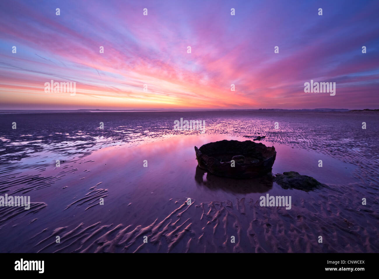 An old rusty bucket lies in a pool of water at sunrise on the beach at ...