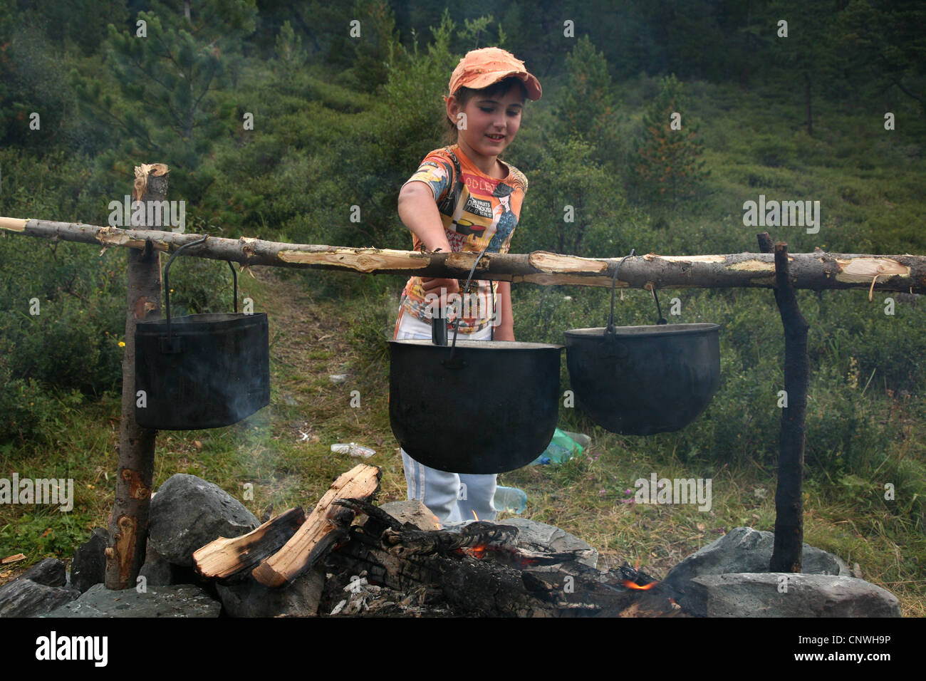 Young girl cooking on the campfire during a trekking in the Altai ...