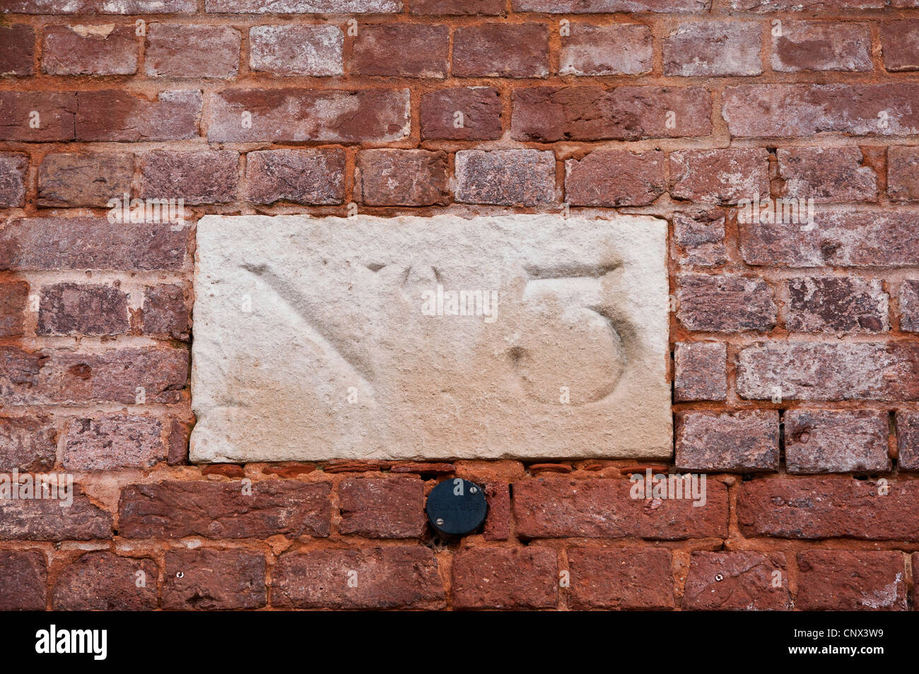 Old, worn sandstone block inserted into a brick wall, inscribed with No ...
