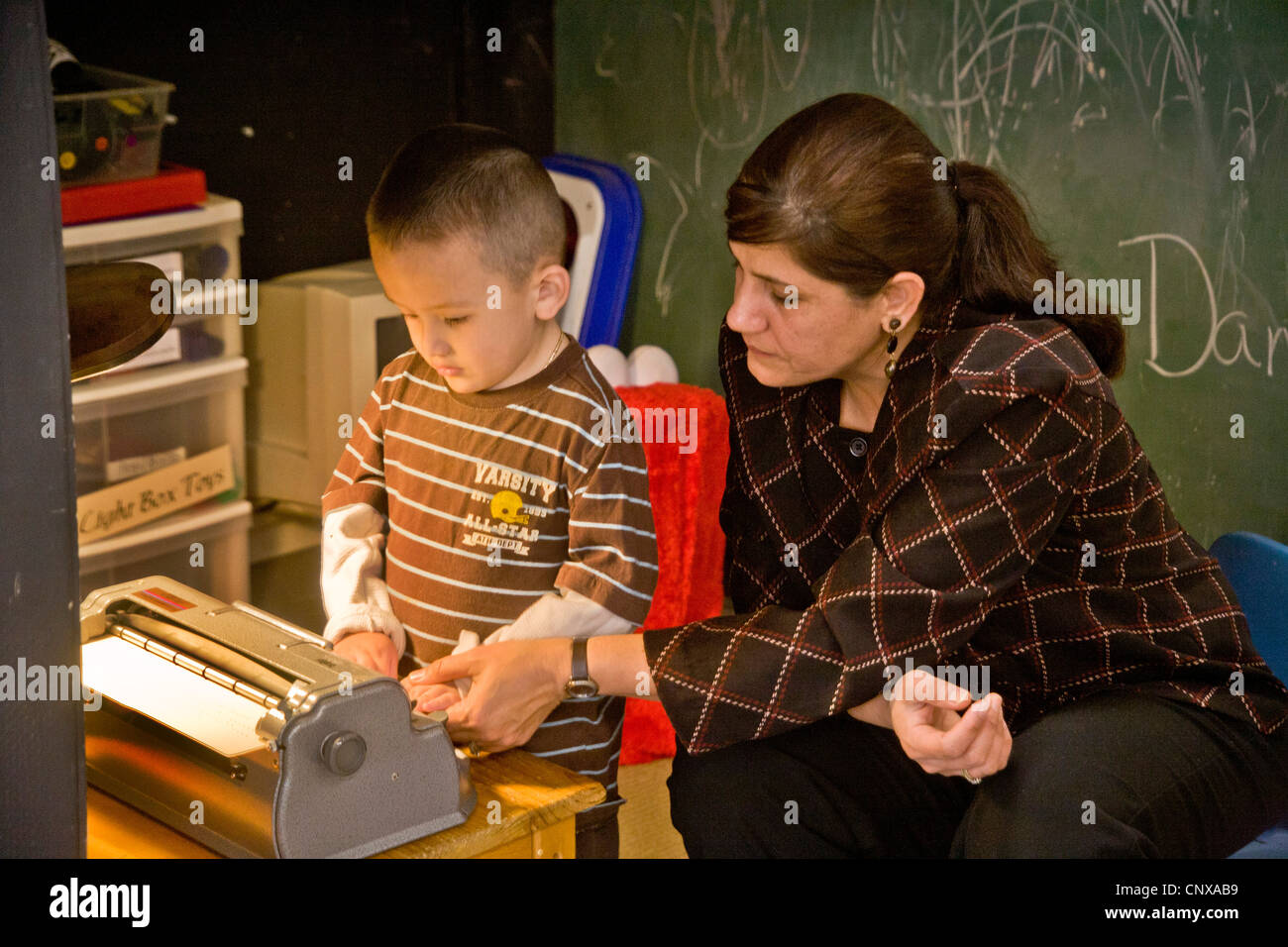 With the help of a trained staff member a blind boy types on a Braille ...