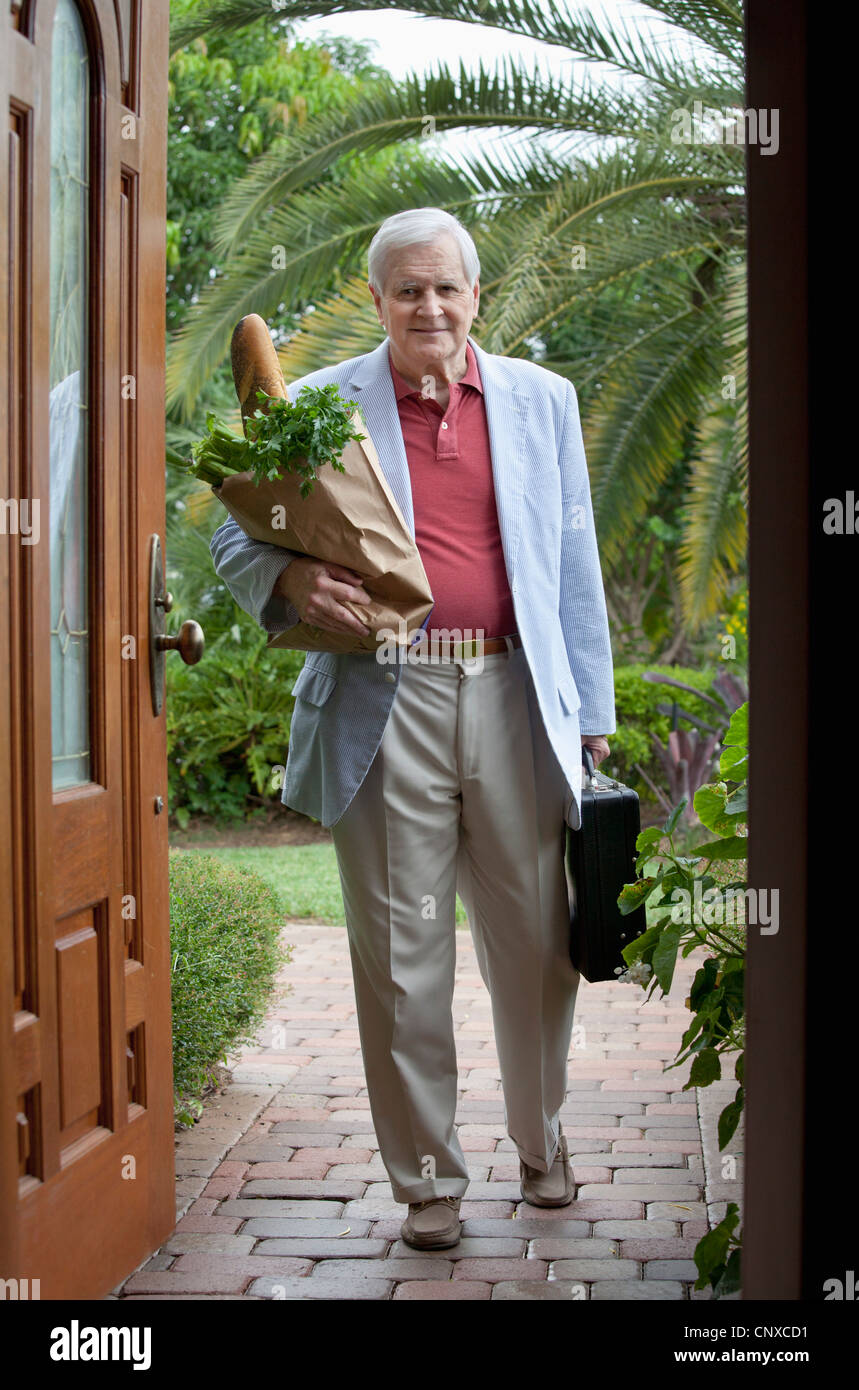 A senior man arriving home with a bag of groceries and a briefcase ...