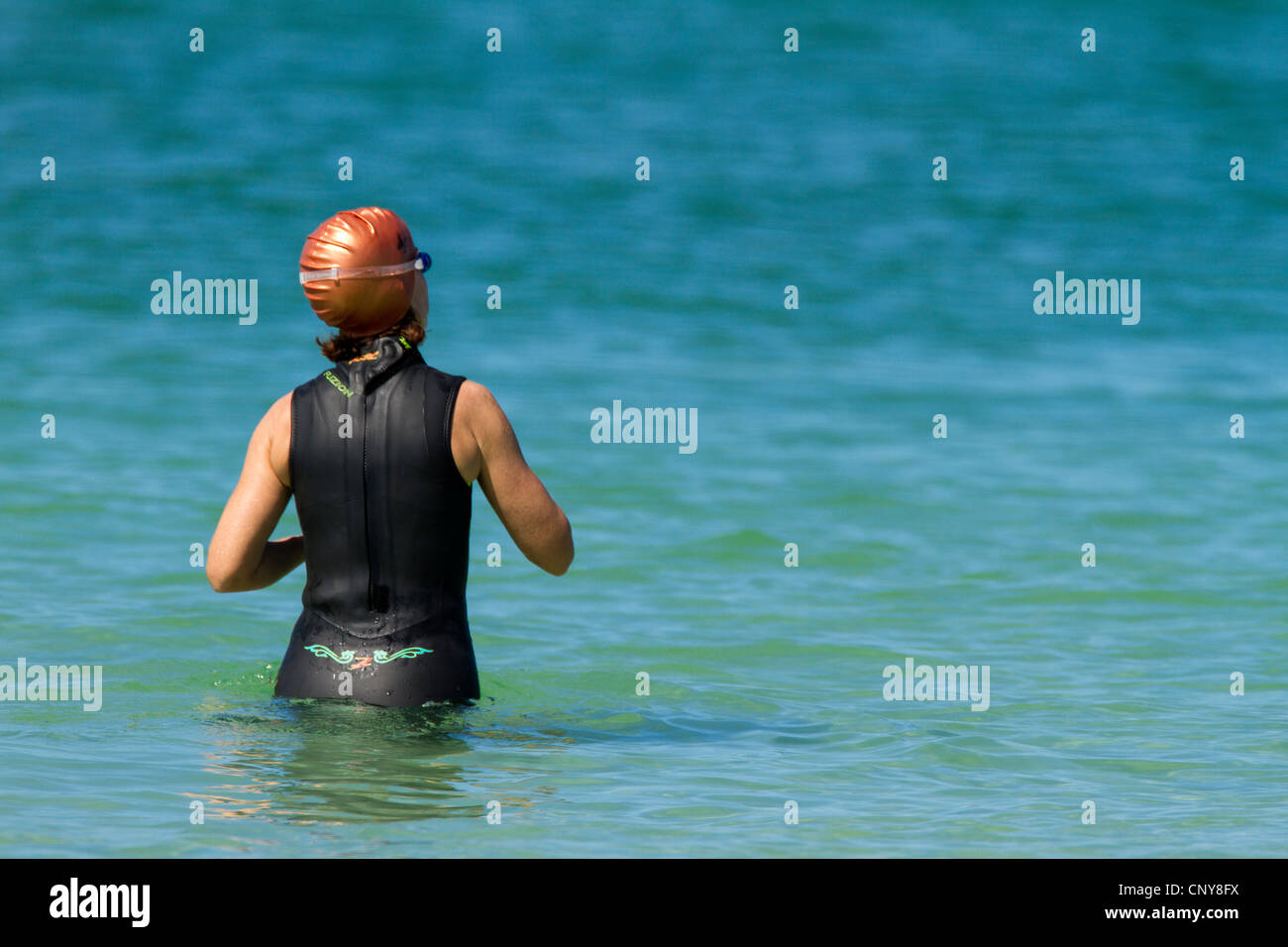 Female swimmer wearing a swimming cap and suit stands in the blue water ...
