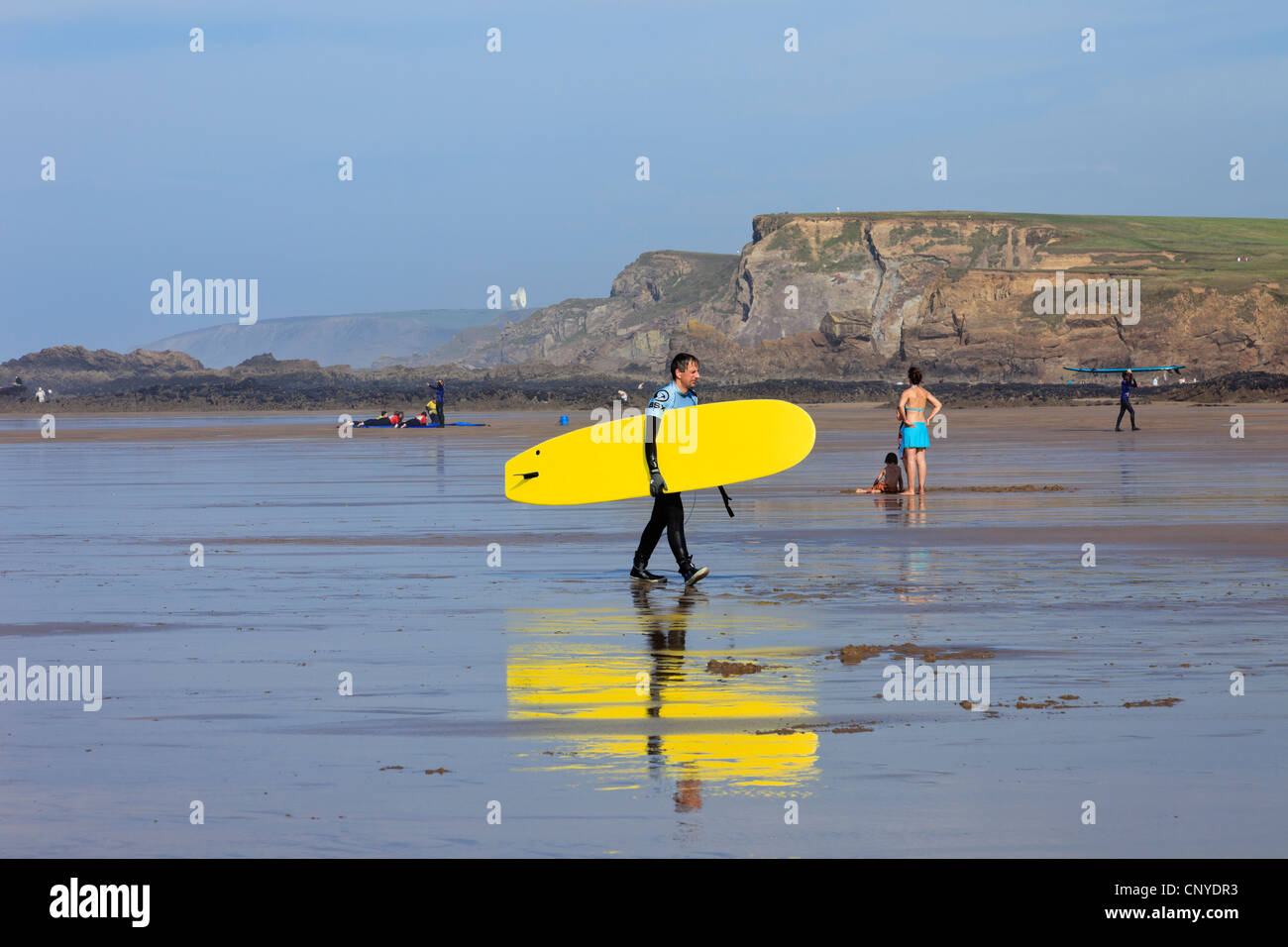 Surfer carrying a yellow surfboard across Crooklets Beach with ...