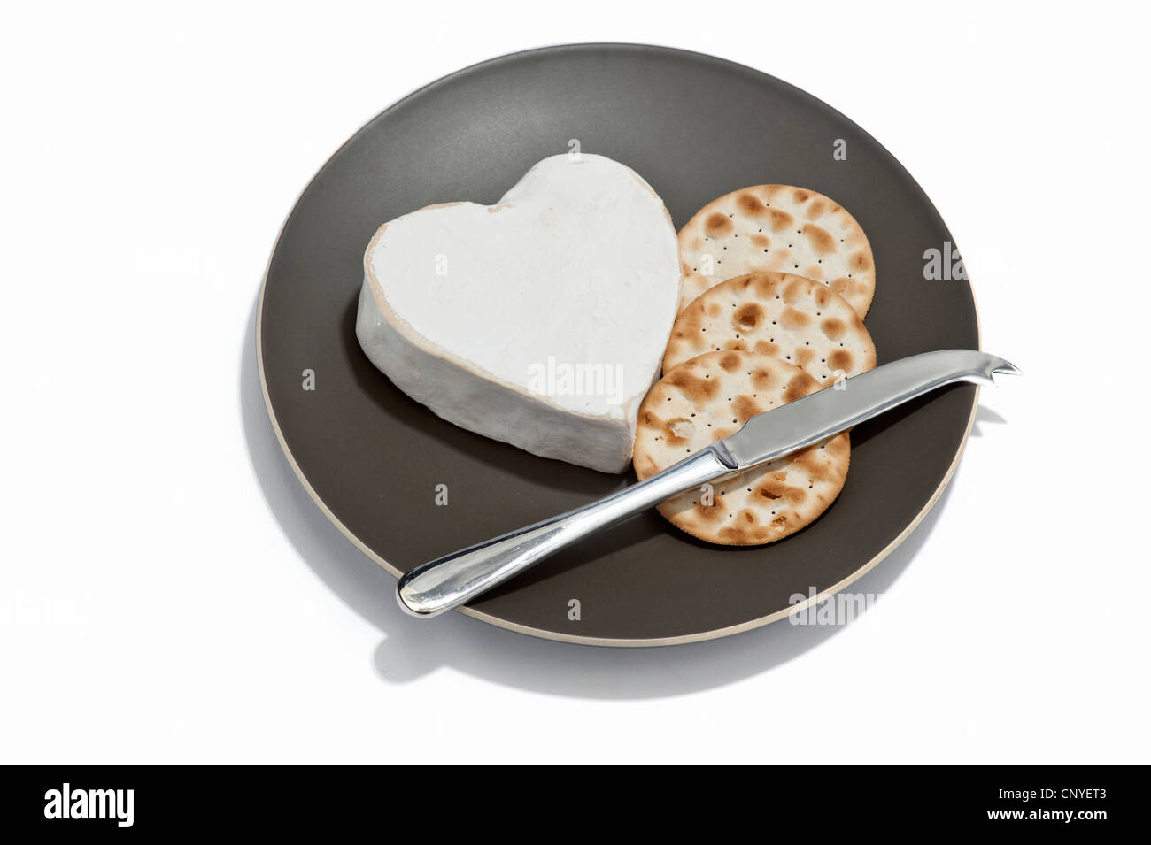 A heart shaped cheese with crackers and cheese knife on a plate Stock ...