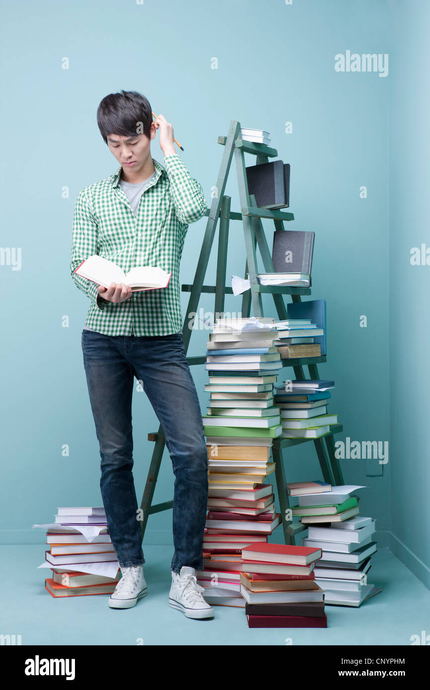 A man reading a book by the piled books and ladder Stock Photo - Alamy