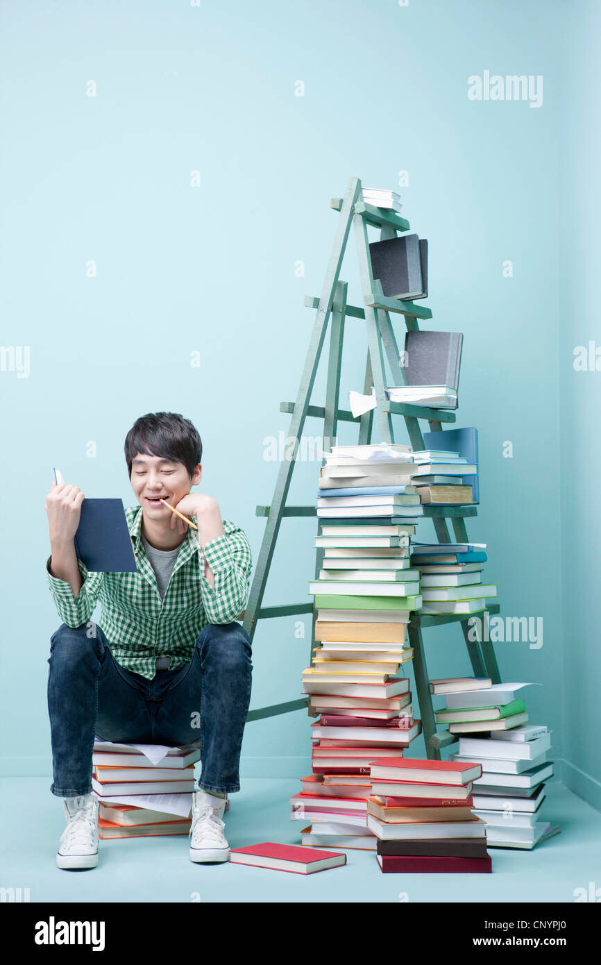 A man reading a book by the piled books and ladder Stock Photo - Alamy