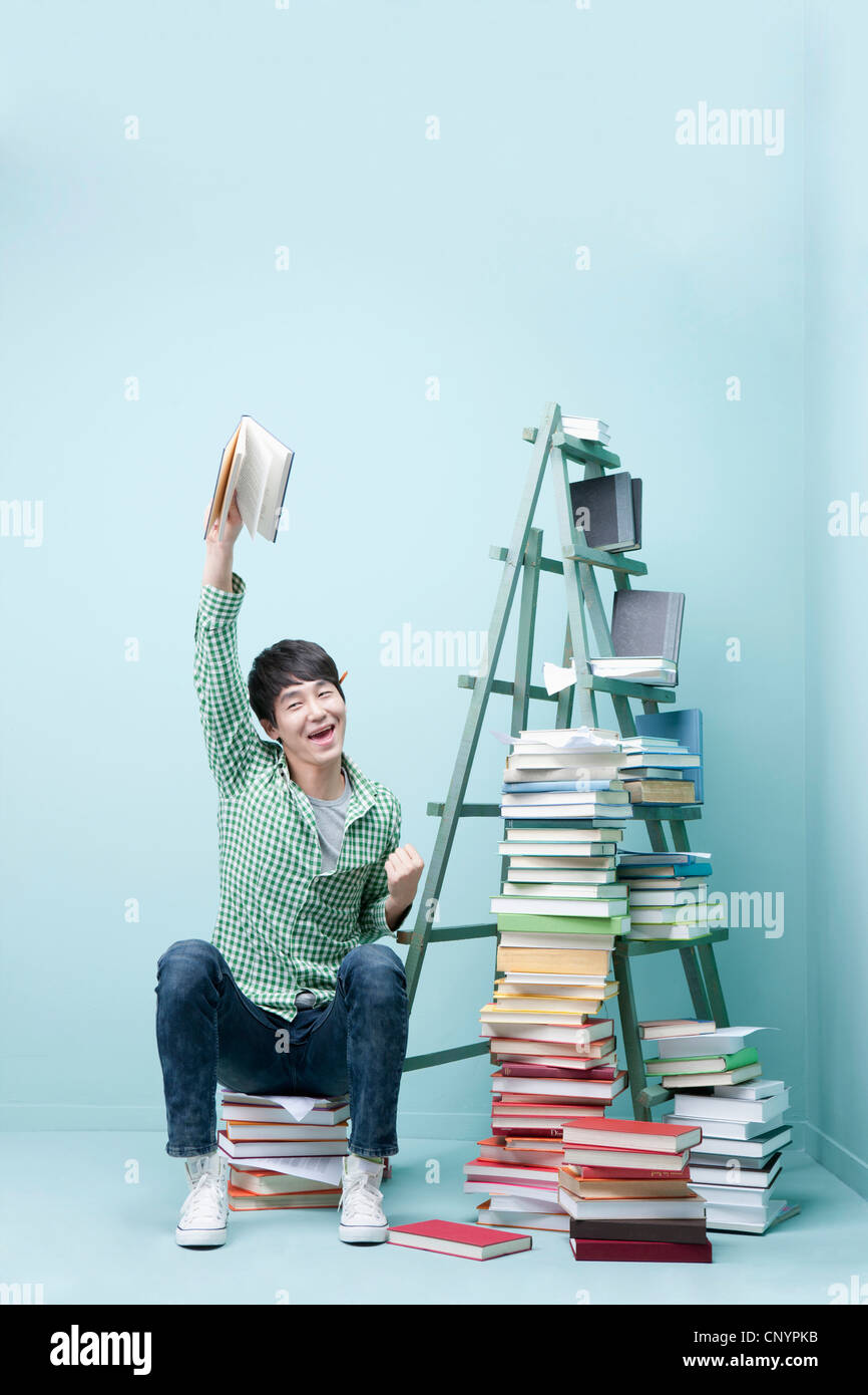 A man holding up a book by the piled books and ladder Stock Photo - Alamy