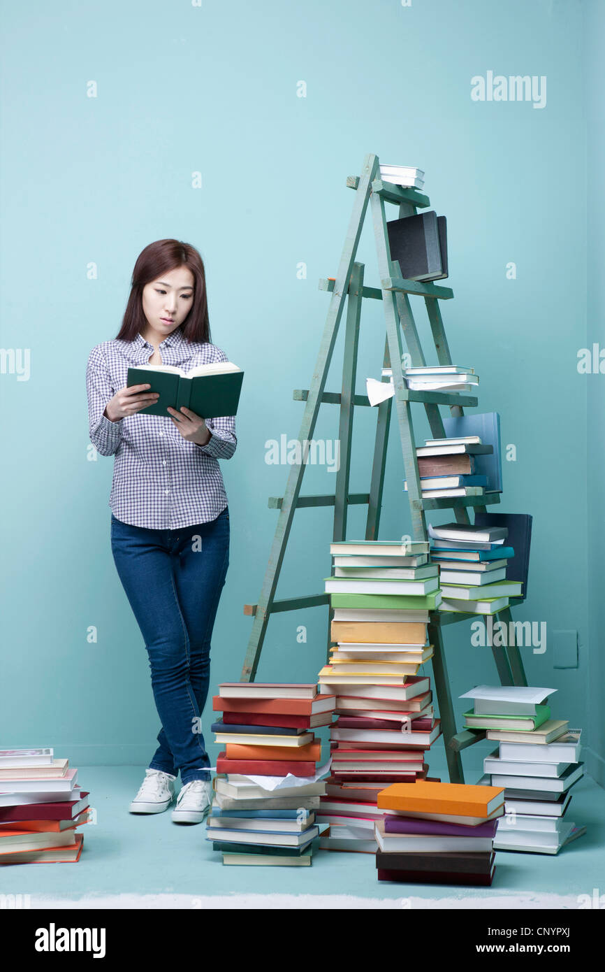 A woman reading a book by the piled books and ladder Stock Photo - Alamy