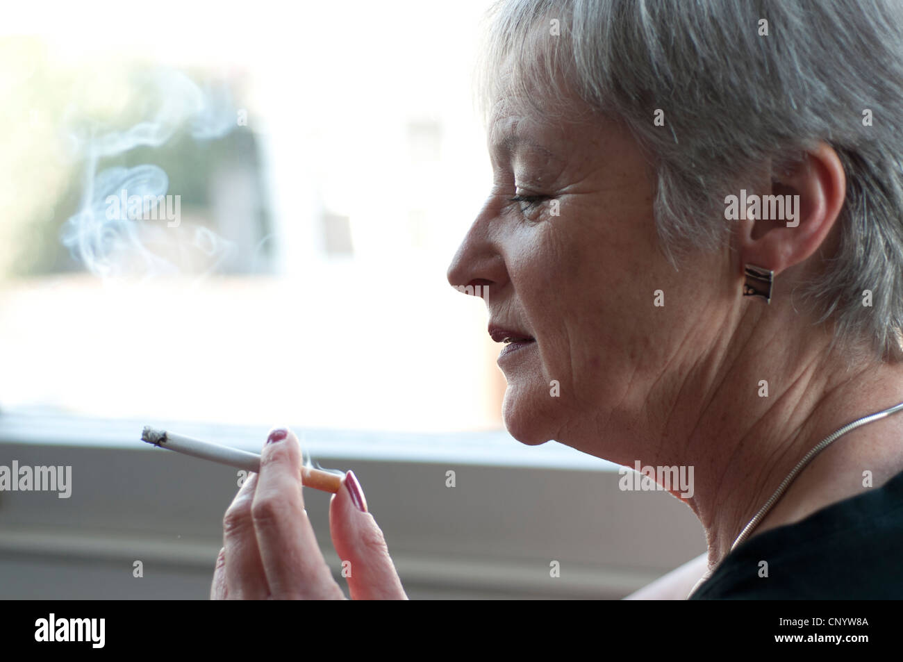 Middle aged woman near window smoking a cigarette Stock Photo - Alamy