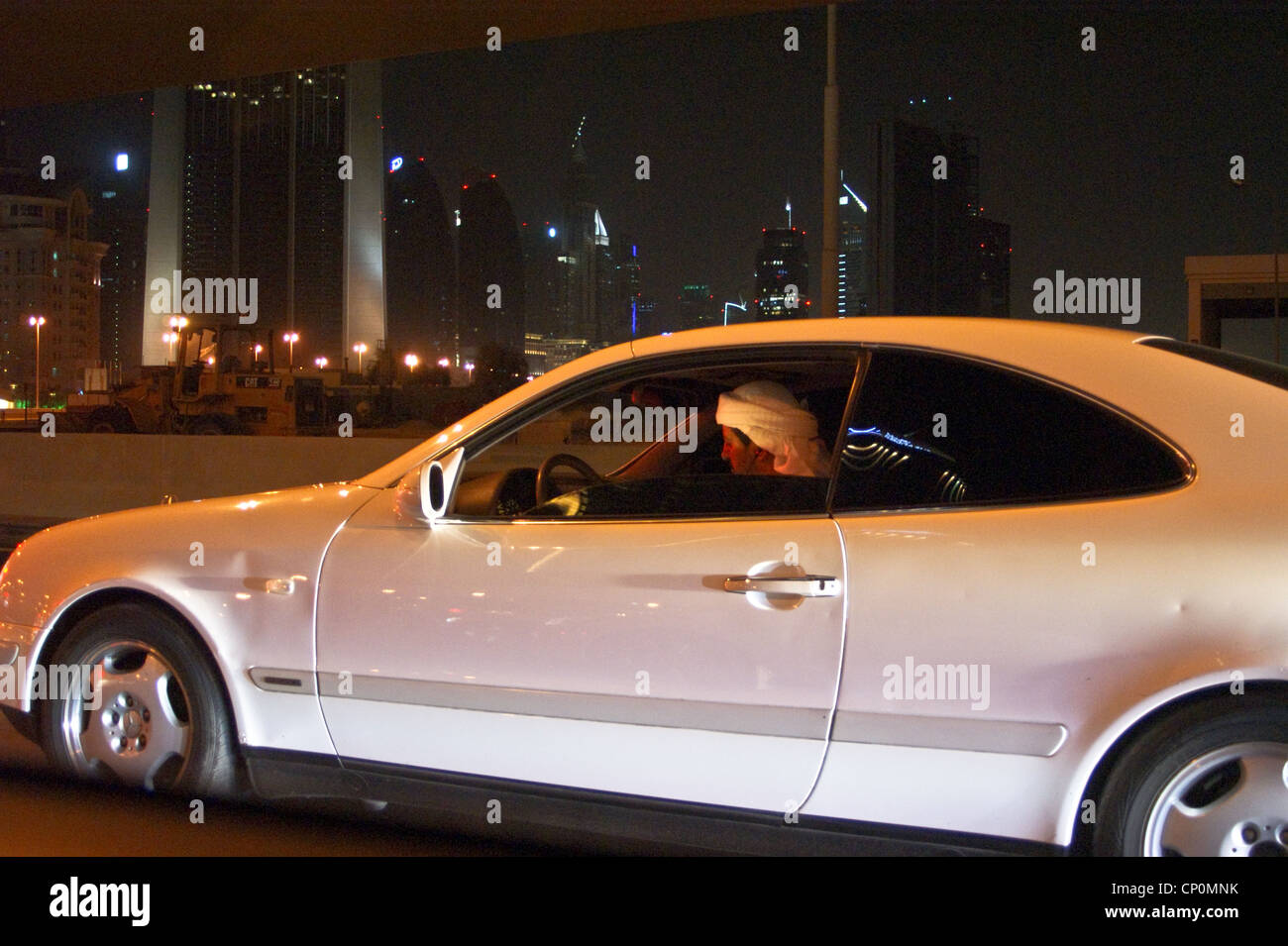 A man in traditional Arab dress driving a Mercedes, at night in Dubai ...
