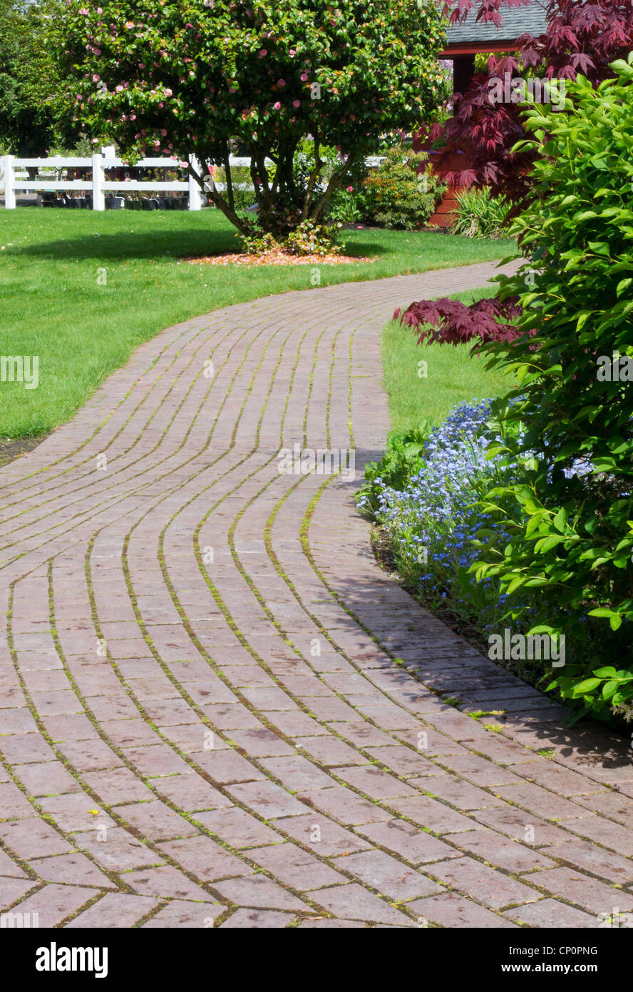 A winding paved garden path with white fence and red shed Stock Photo ...