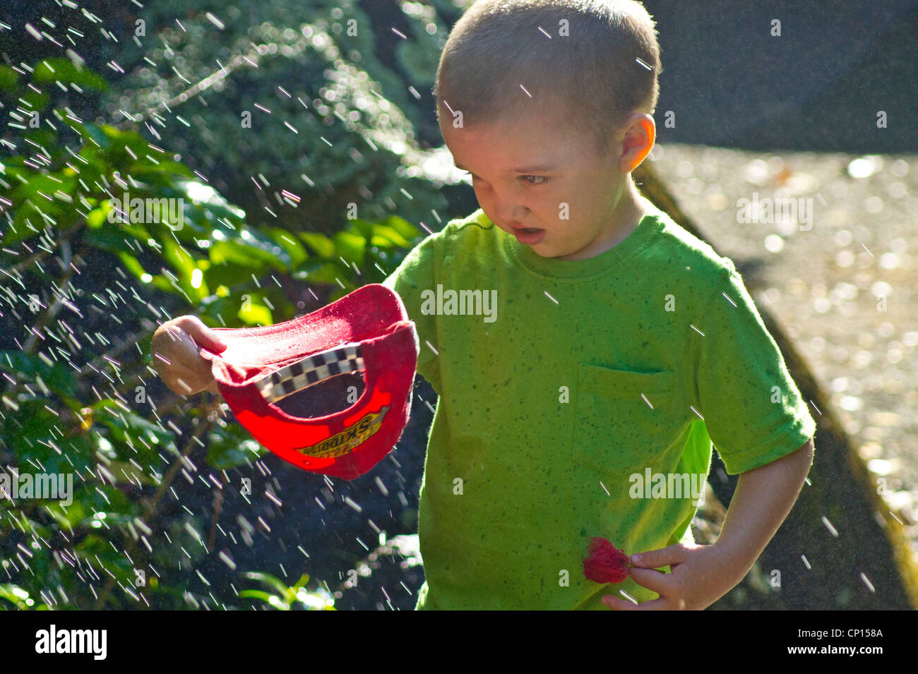 4 yr old autistic boy catching water from sprinkler in hat Stock Photo ...