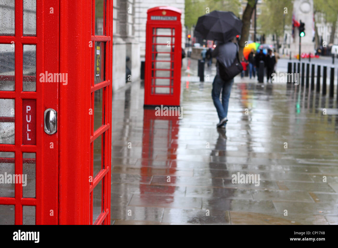 people walking in the rain passed red telephone boxes Stock Photo - Alamy