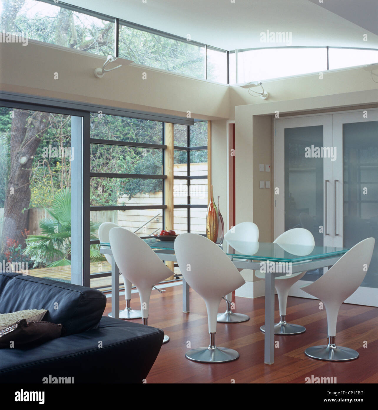 Glass table and retro style chairs behind leather sofa in open plan ...