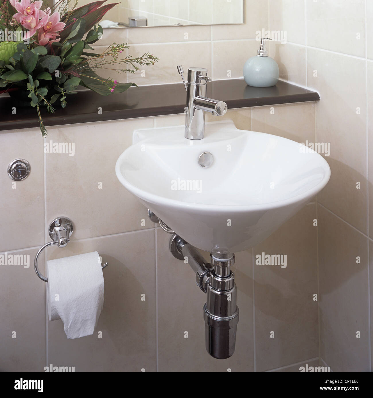 Circular wash basin mounted on tiled wall with flowers on shelf Stock ...