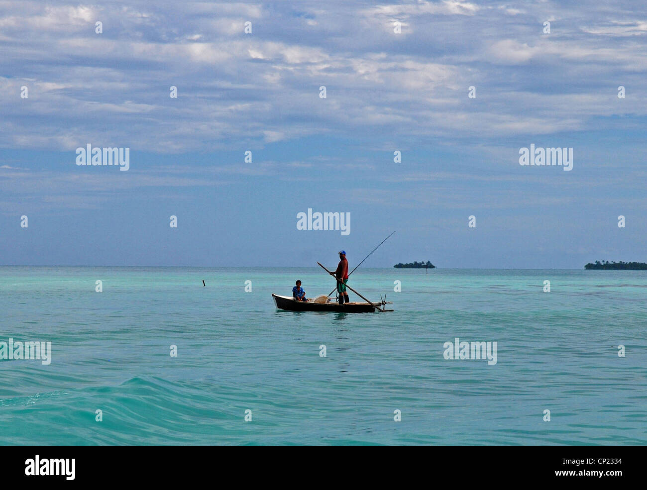 Man and son fishing from a small wooden canoe in a shallow lagoon ...