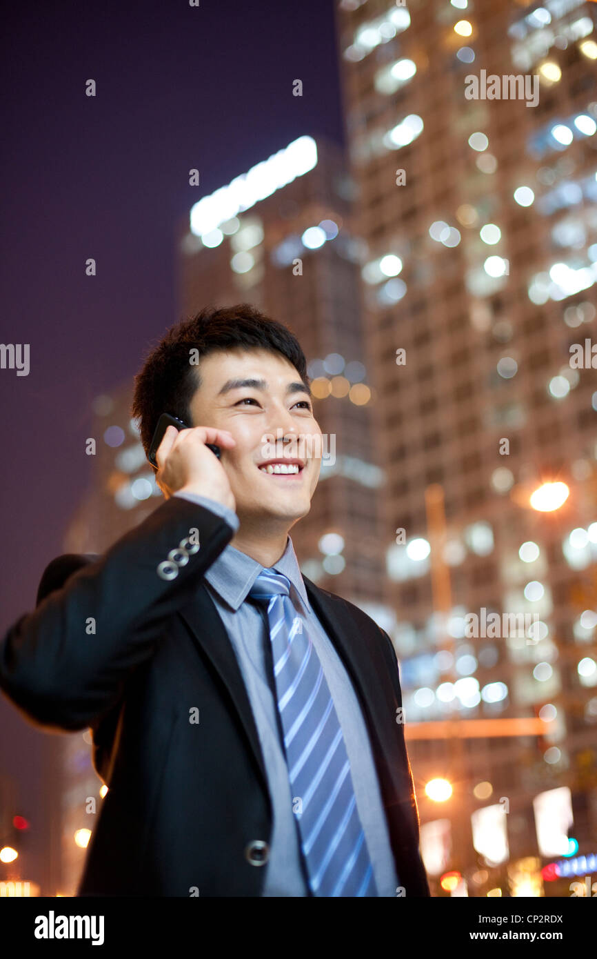 Chinese businessman using cellphone with city lights in the background ...