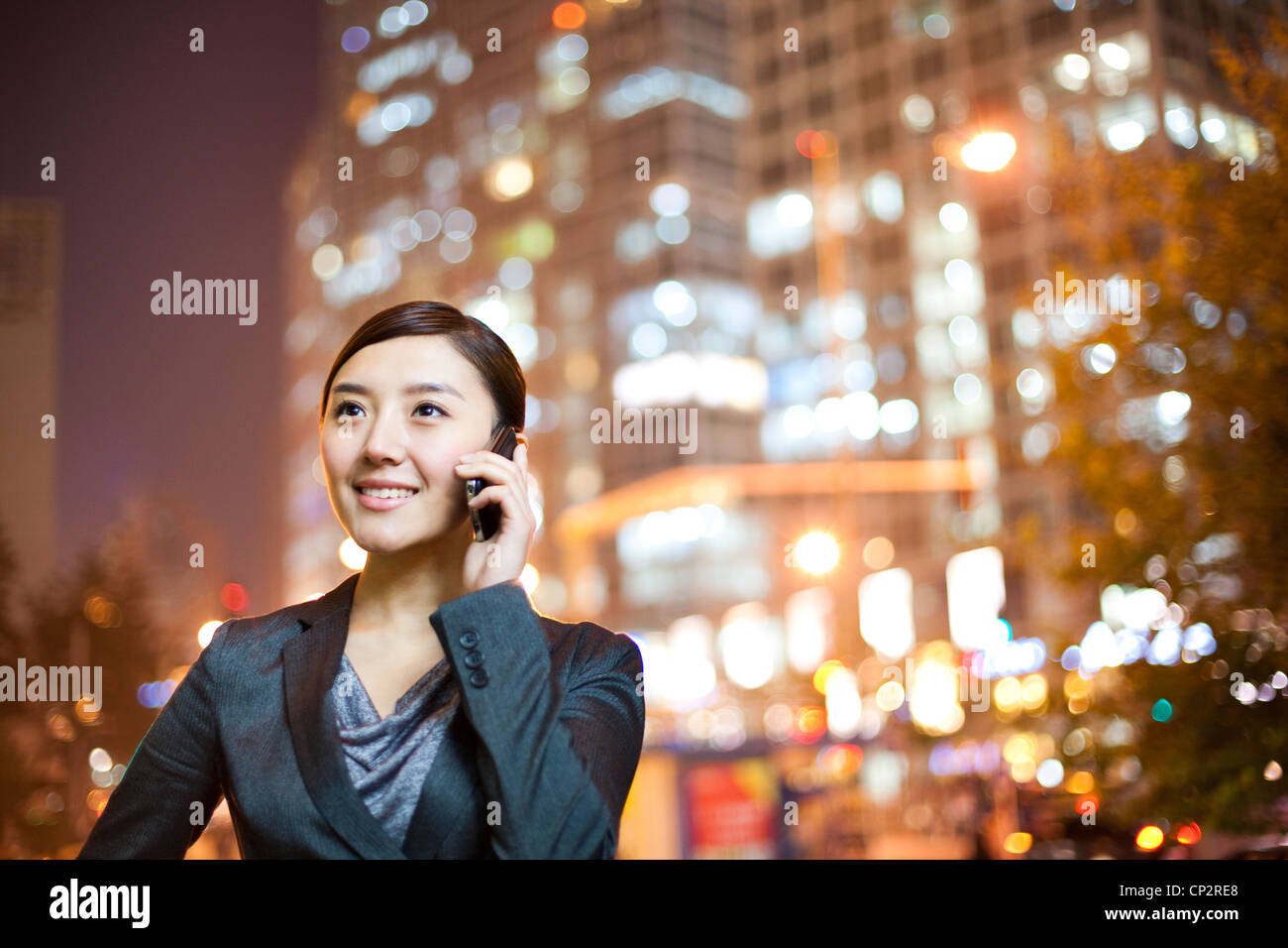 Chinese businesswoman using cellphone with city lights in the ...