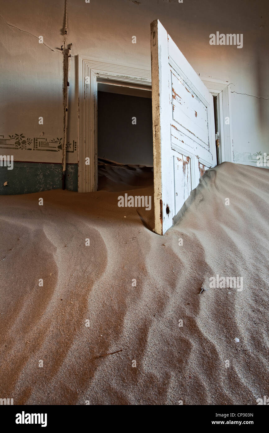 Accumulated desert sand blocks a door inside a house in Kolmanskop ...