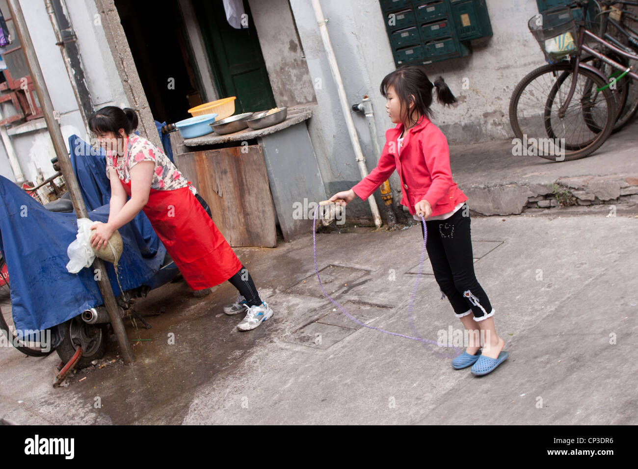 A woman straining water (probably from soya beans), while a girl skips ...