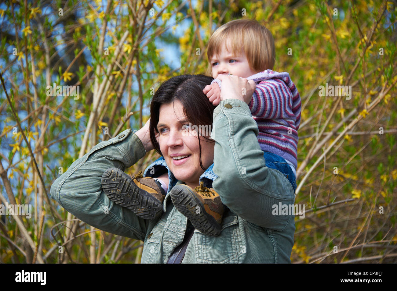 Mother carrying child baby girl daughter on shoulders in park in spring ...