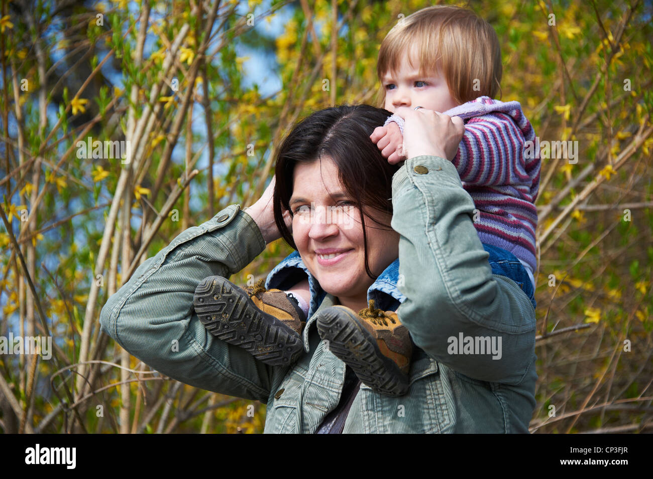 Mother carrying child baby girl daughter on shoulders in park in spring ...