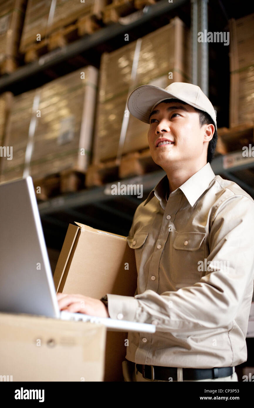 Male Chinese warehouse worker using a laptop Stock Photo - Alamy